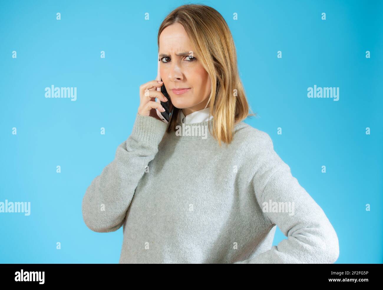 Young woman disgusted using mobile phone isolated on blue background ...