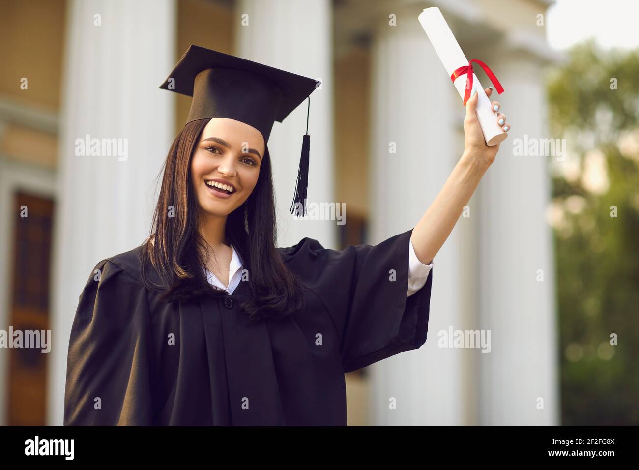 Happy girl university graduate standing and holding diploma in raised ...
