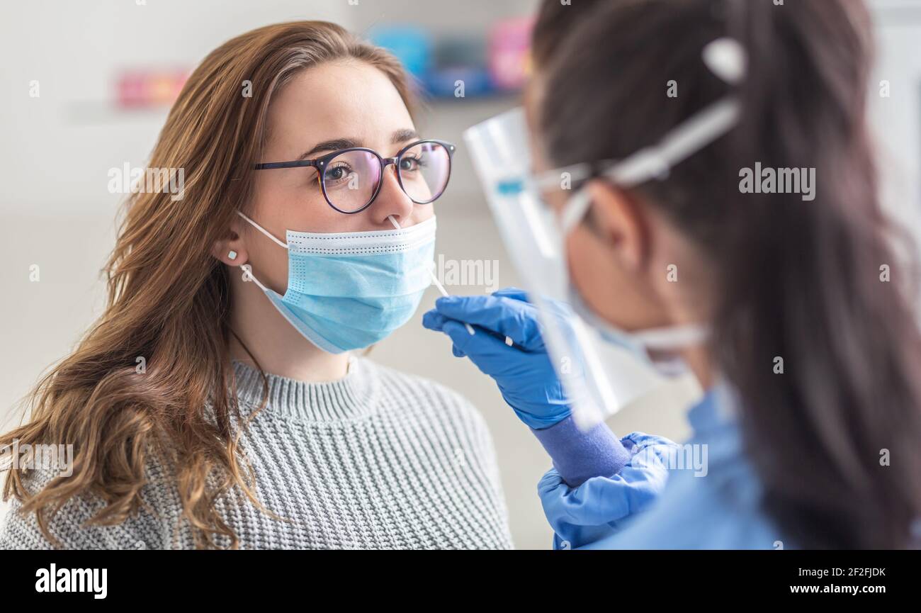 Female patient wearing mask over mouth is having sample taken from nose ...