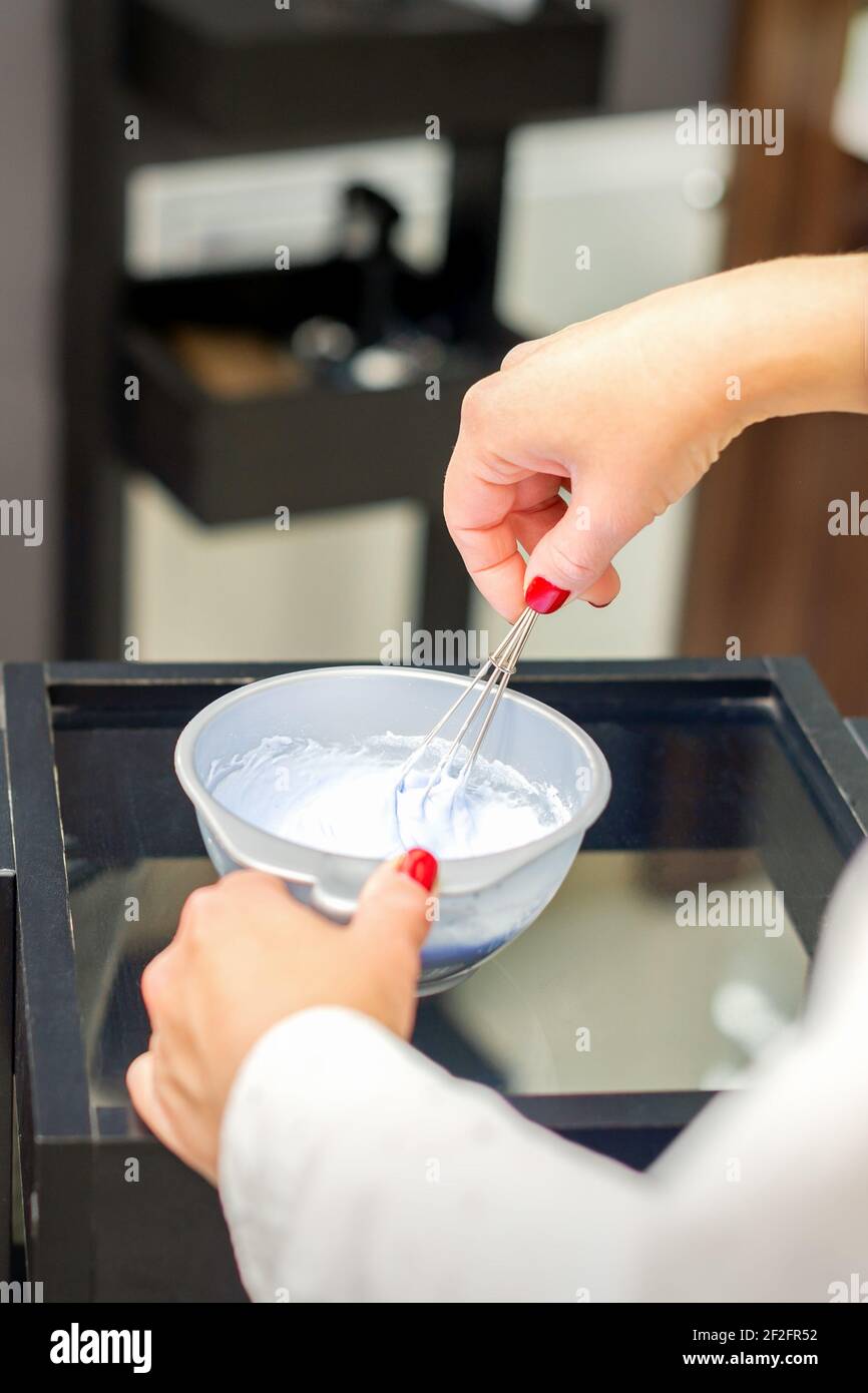 The hairstylist makes a white color dye mix for coloring hair at a ...