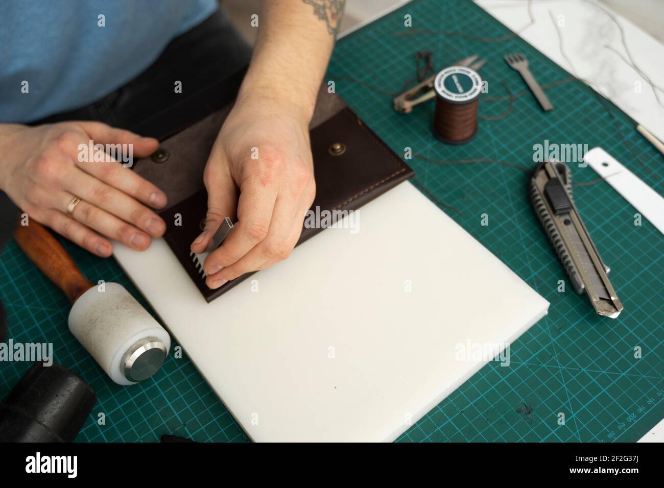 Mens hand holding a leather carving hammer and steel chisel hole punch ...