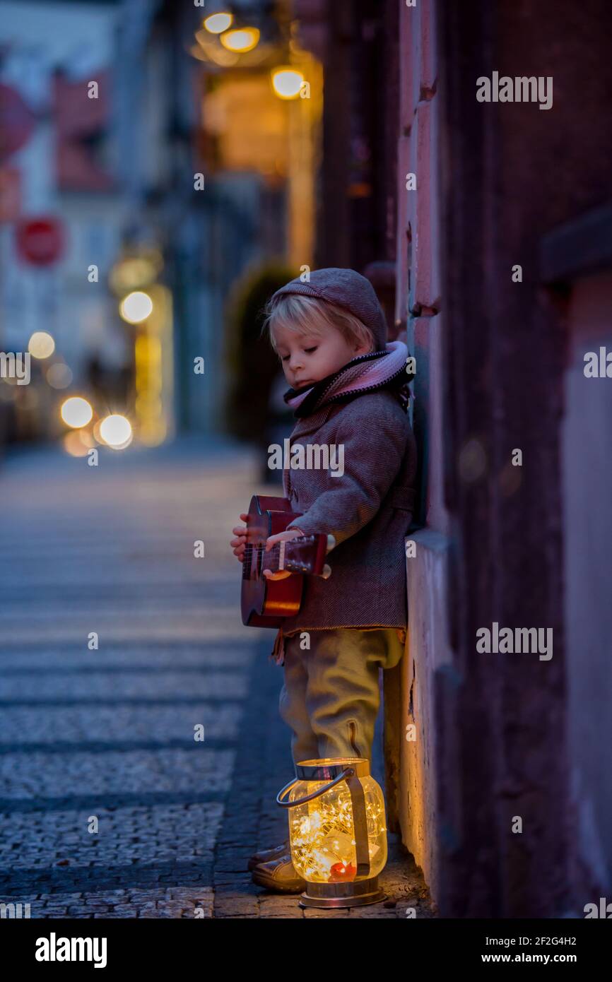 Sweet toddler boy, playing guitar at night in the city with teddy bear ...