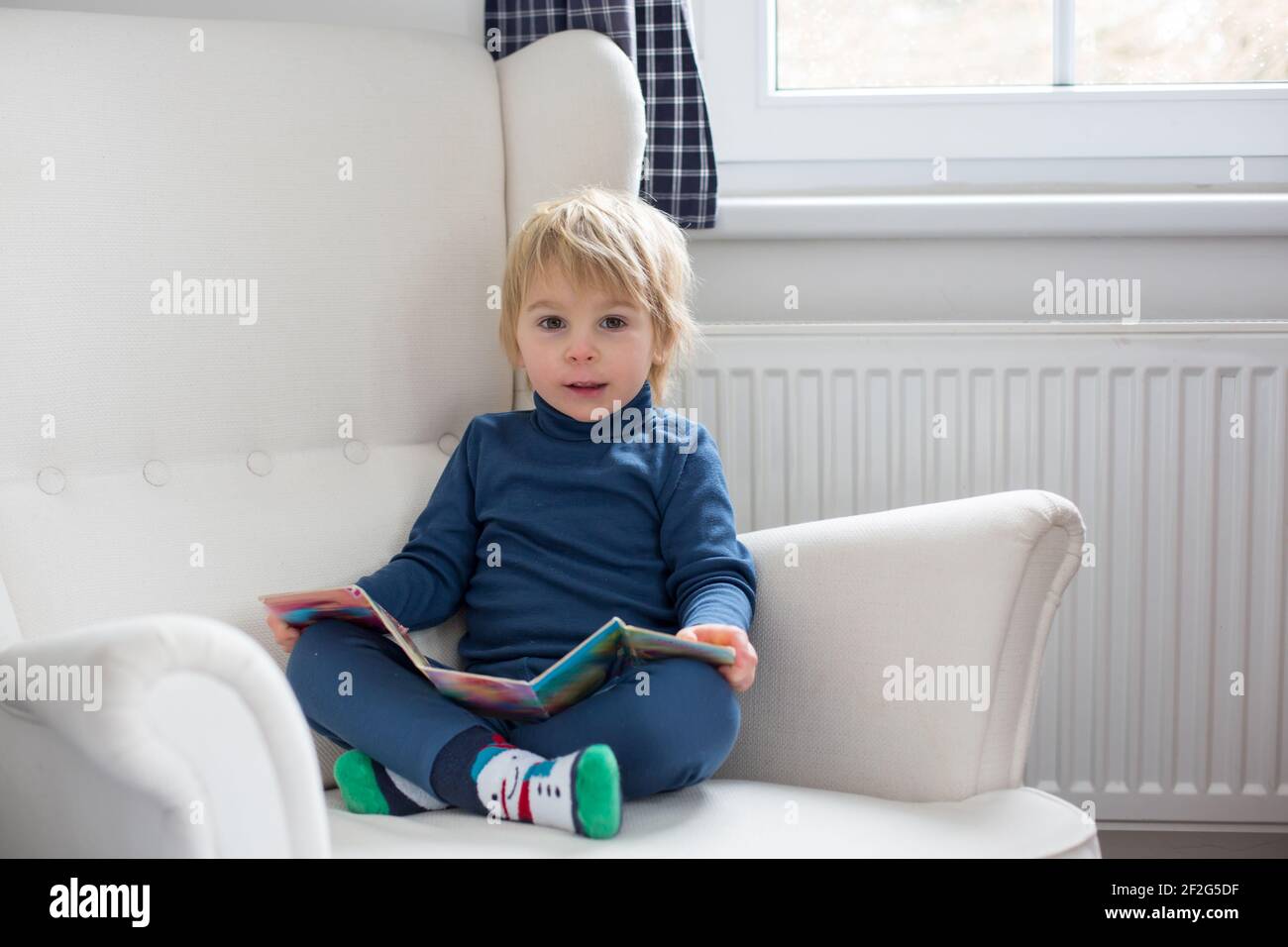 Mother and child, toddler boy, reading a book, sitting in a cozy ...