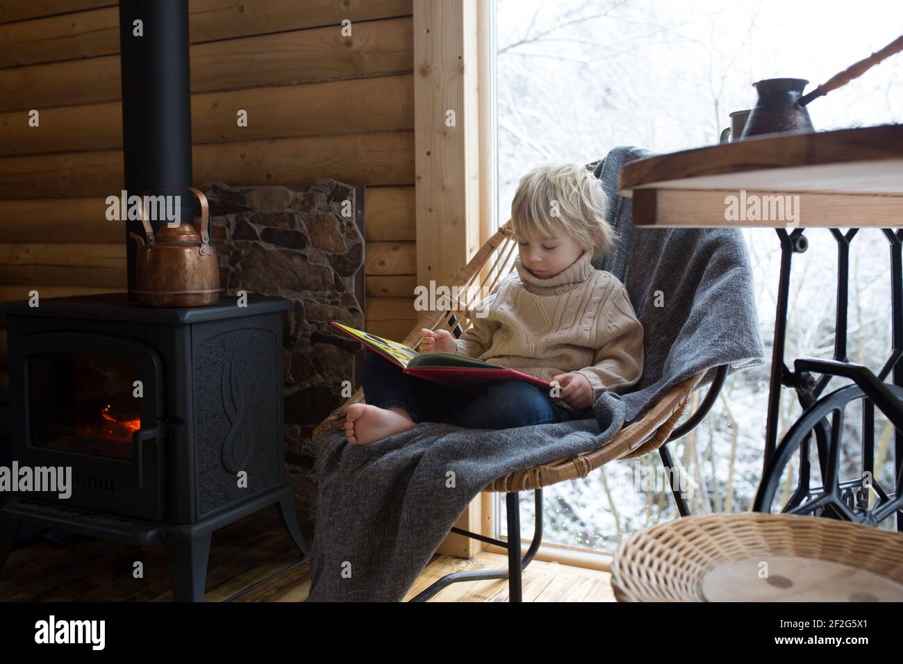 Cute toddler child in a little fancy wooden cottage, reading a book ...