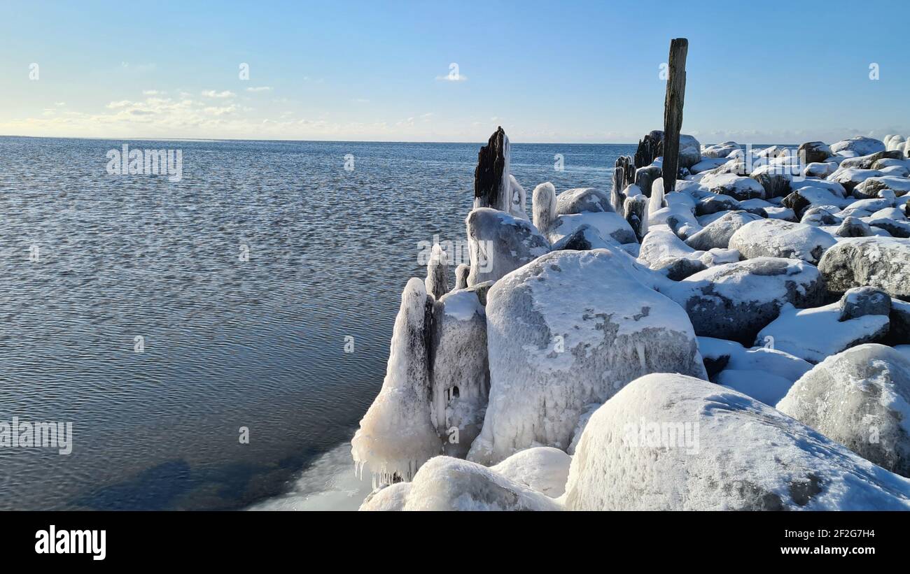 frozen wooden poles on the sea shore with blue water and blue sky on a ...