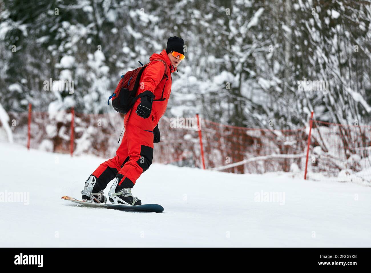 Male snowboarder in a red suit rides on the snowy hill with snowboard ...