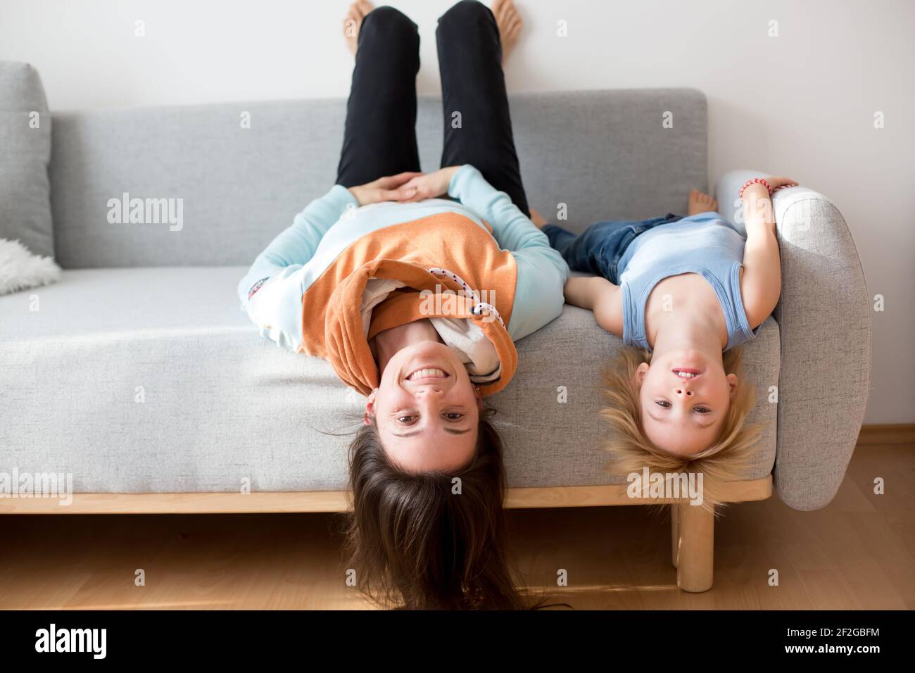 Mother and toddler child, hanging upside down from a couch at home ... Mother and toddler child, hanging upside down from a couch at home ...