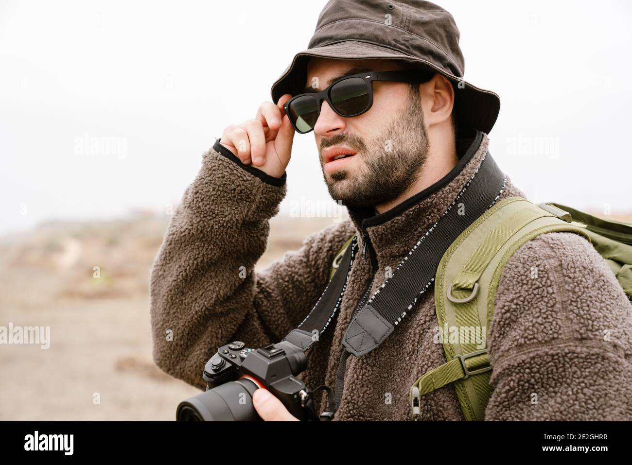 Focused handsome photographer in sunglasses walking with digital camera ...