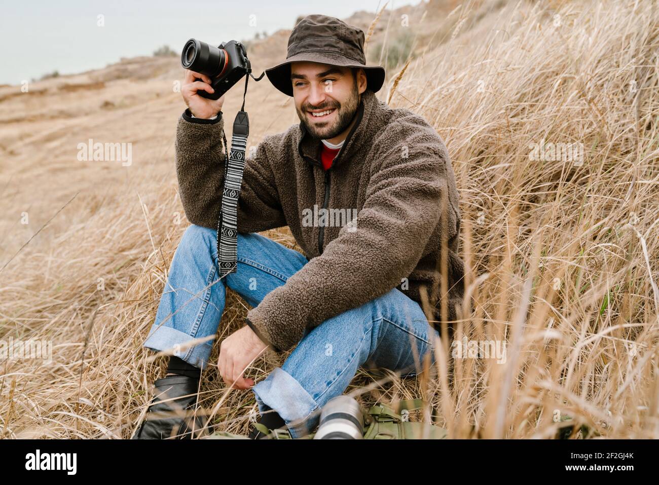 Happy handsome photographer with camera smiling while sitting outdoors ...