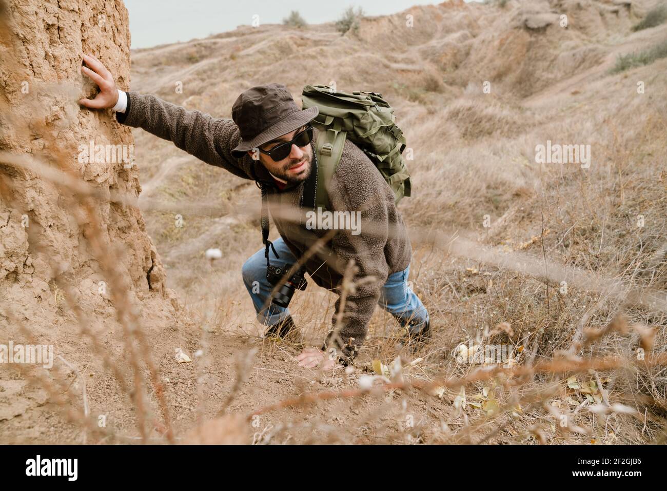 Focused handsome photographer with camera climbing on hill outdoors ...