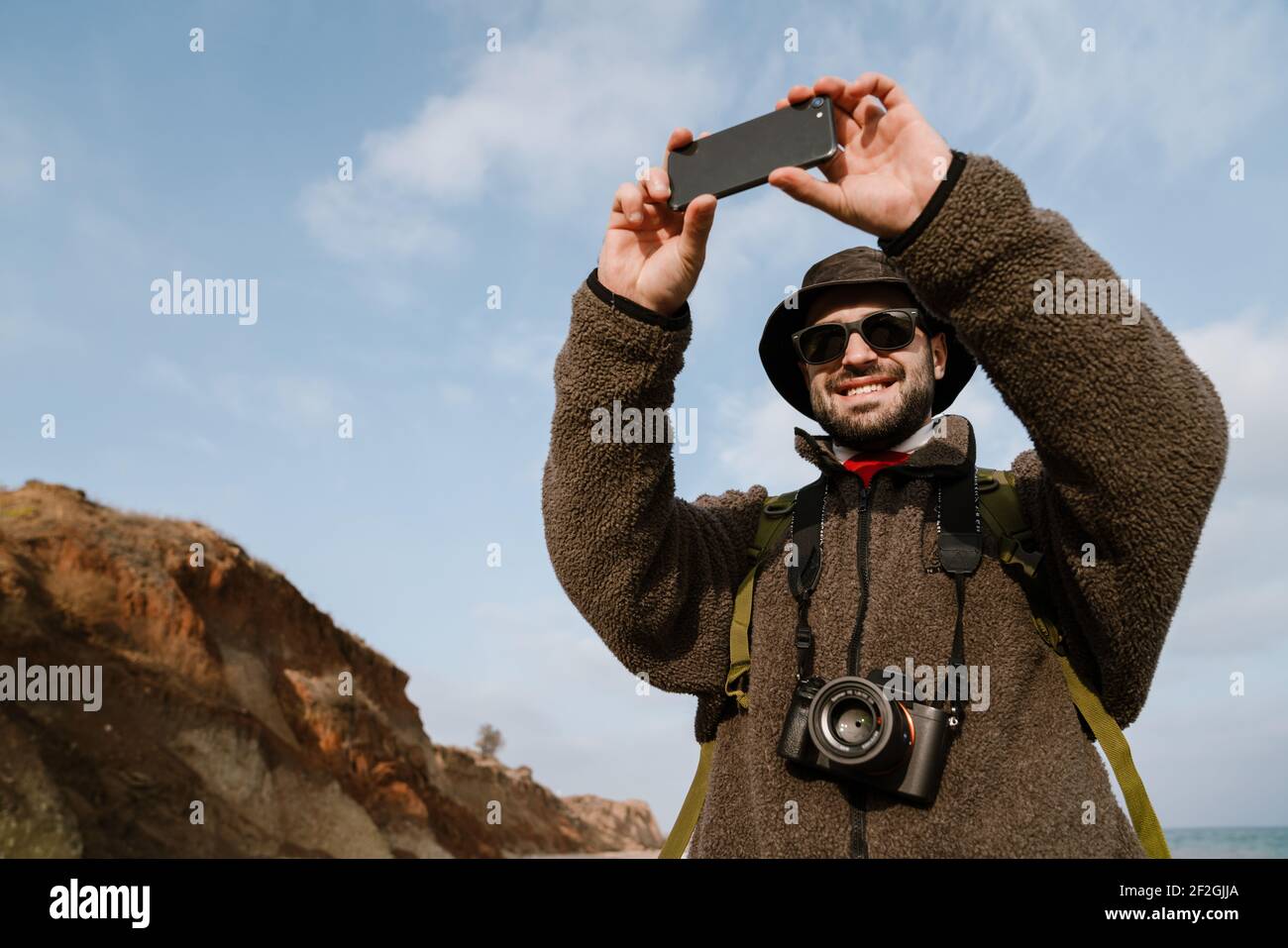 Happy unshaven man smiling while taking selfie on mobile phone at beach ...