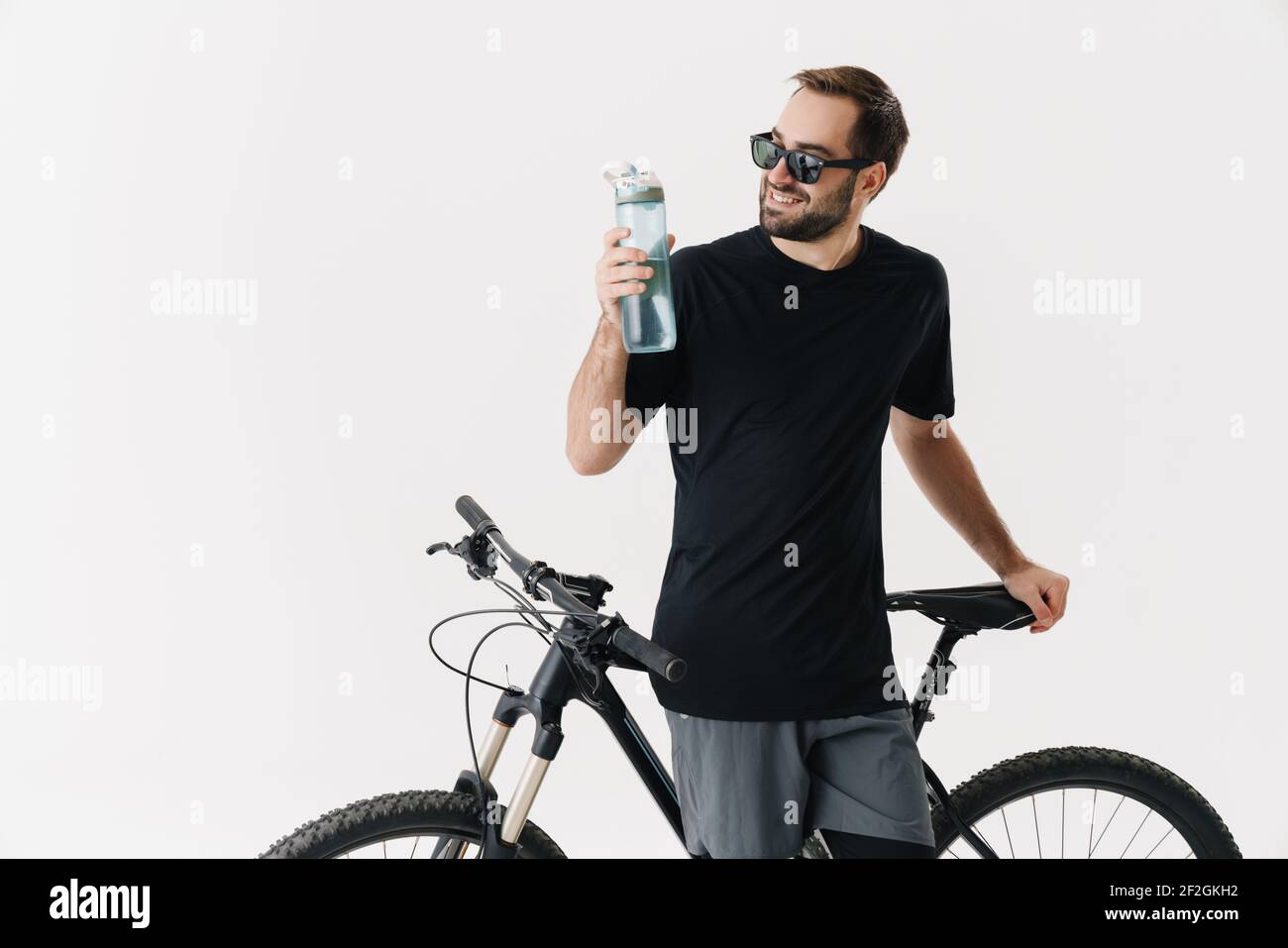 Happy rider man drinking water while posing with his bicycle isolated ...