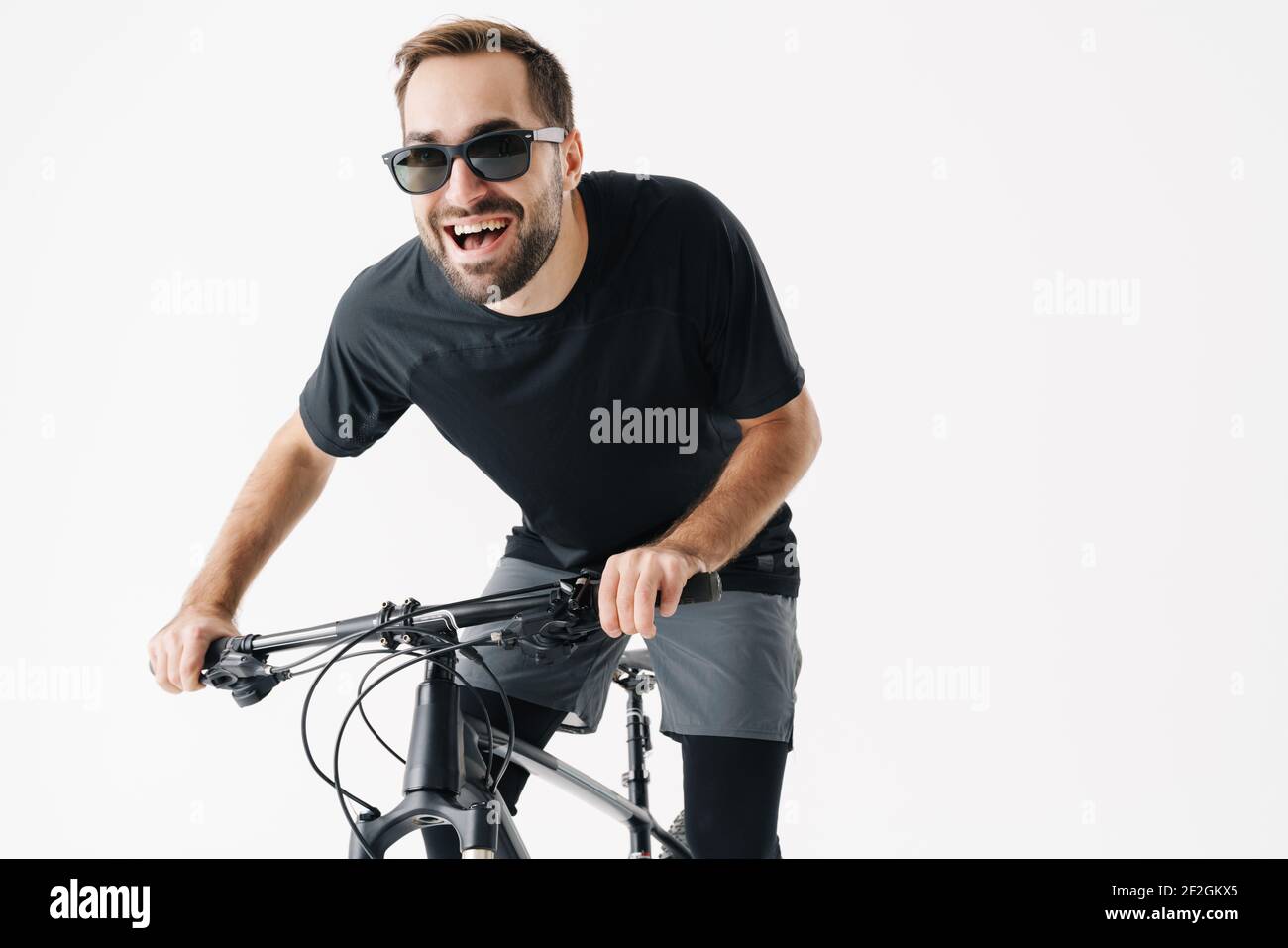 Excited young sportsman in sunglasses riding his bicycle isolated over ...