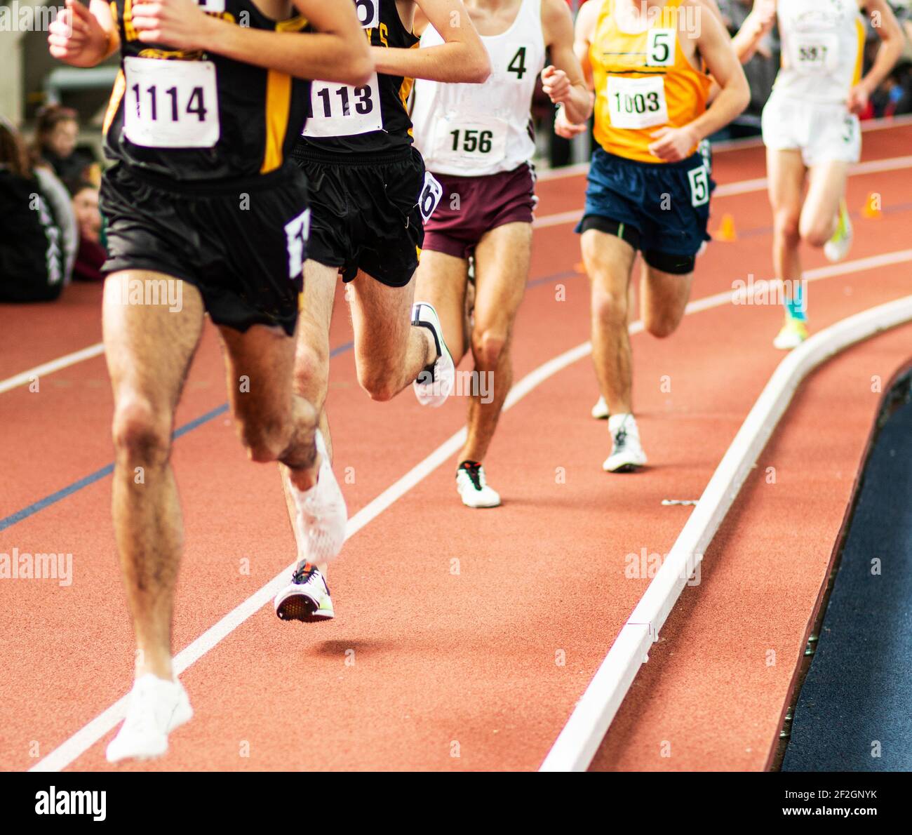 A line of runners on an indoor track racing the mile in a competitive ...