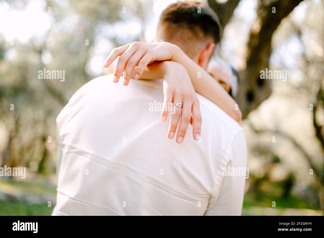 The bride gently hugs the groom in the park, wrapping her arms around his neck, close-up Stock ...
