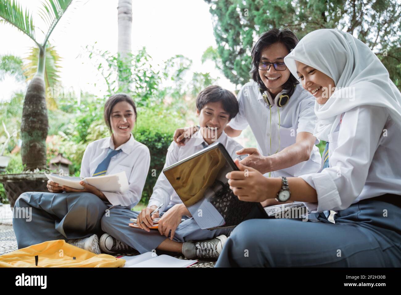 four high school students use laptops during group study with friends ...