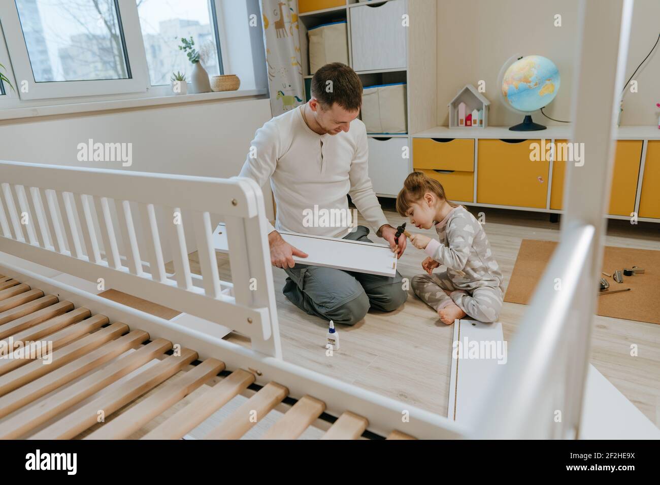 Little 4-years girl helping her father assemble the kids bed using ...