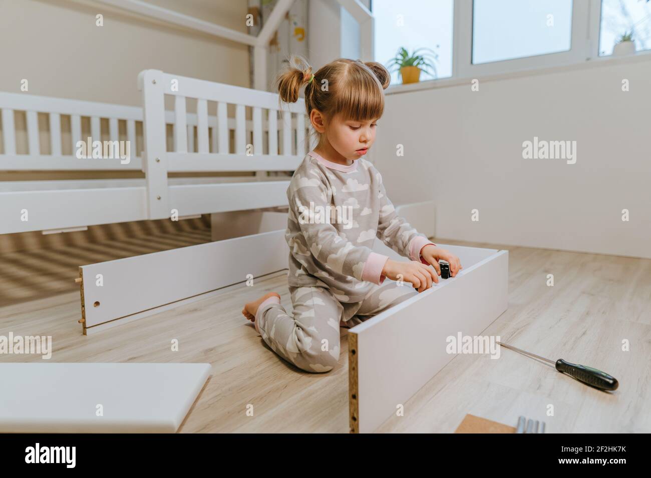 Little 4-years girl assemble the drawer of bed in the kids bedroom ...