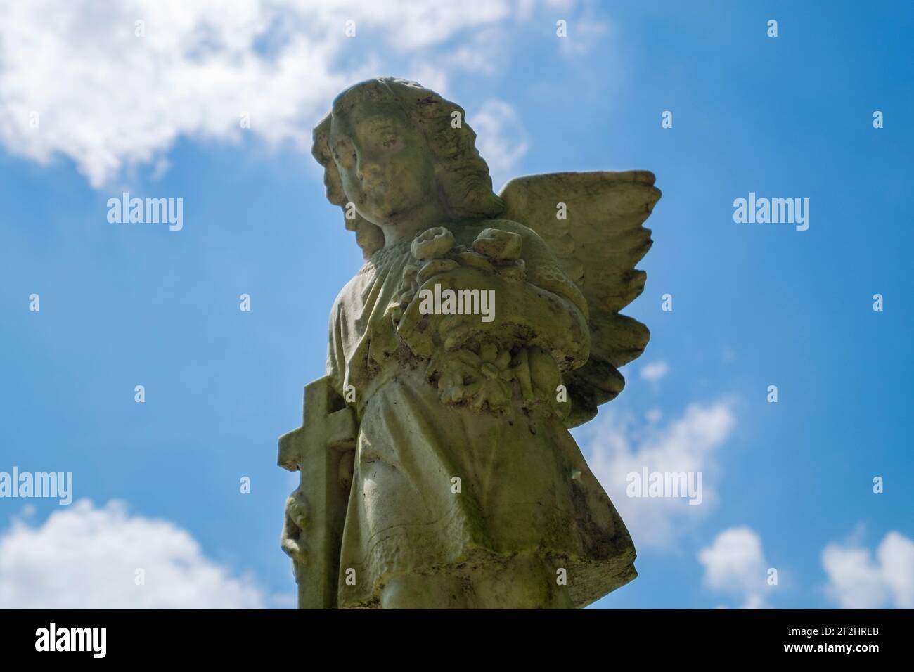 A stone angel with cross figurine against a blue sky and clouds. At Mt ...