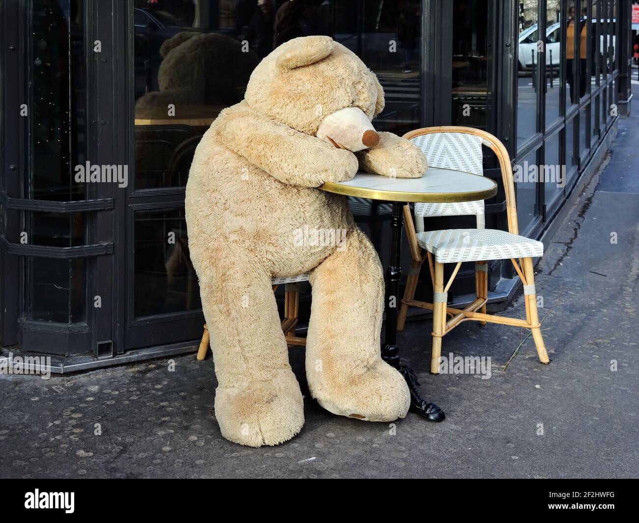 A large teddy bear sits on a chair in a street cafe. Social distancing ...