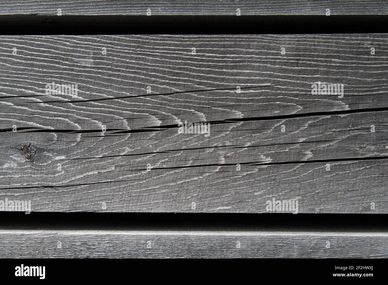 Faded, parallel wooden slats with knotholes and cracks against a black ...