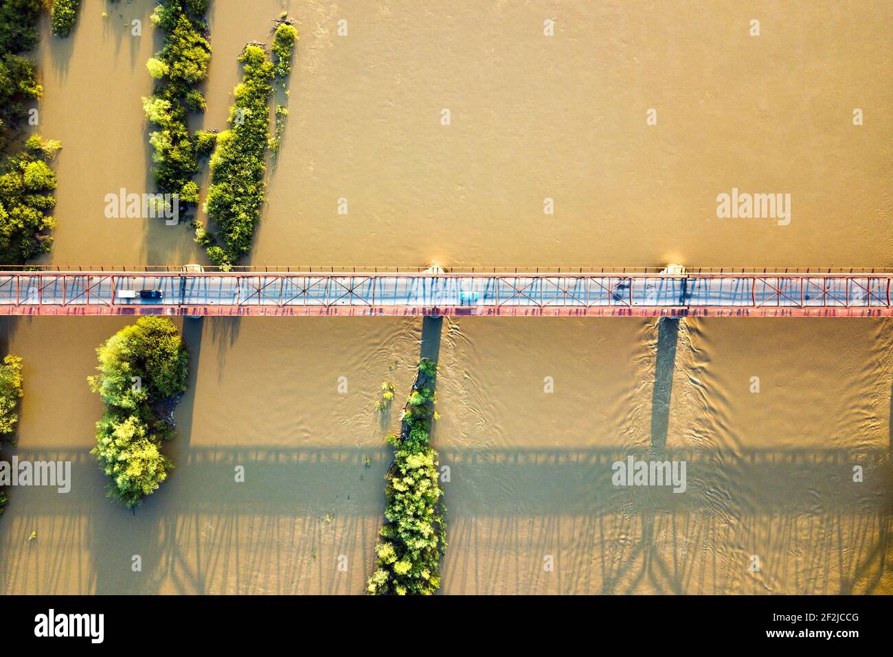Aerial view of a narrow road bridge stretching over muddy wide river in ...