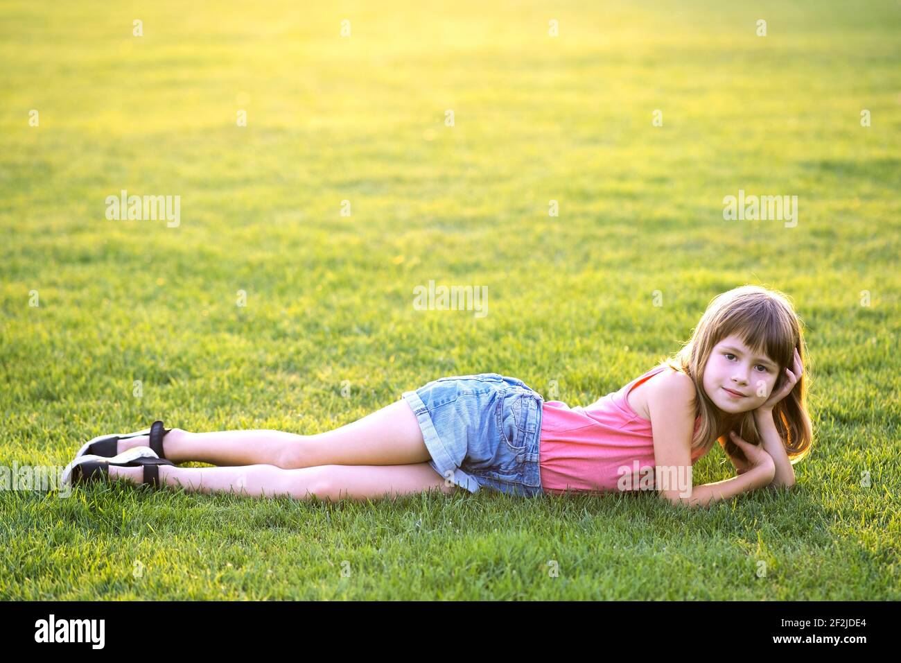 Young pretty child girl laying down on green grass lawn on warm summer ...