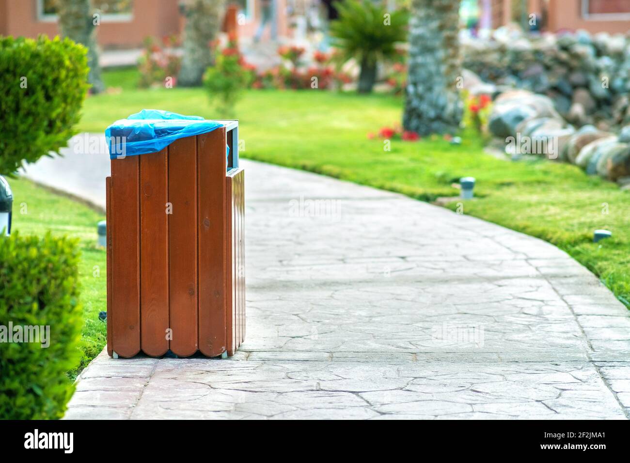 Yellow wooden trash can outdoors on the side of sidewalk in park ...