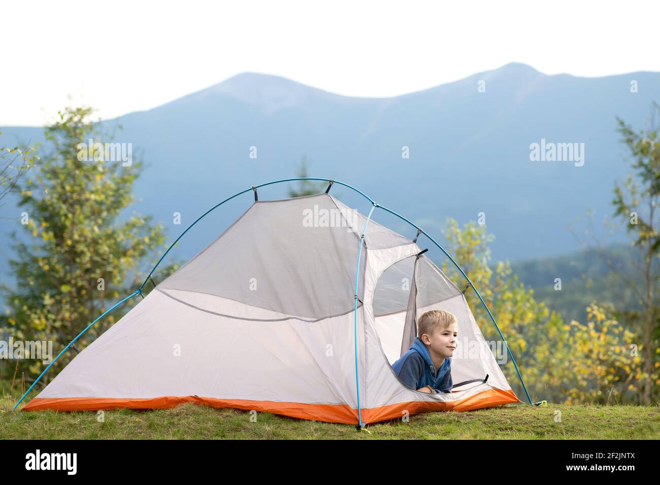 Hiker child boy sitting inside a tent in mountain campsite enjoying ...