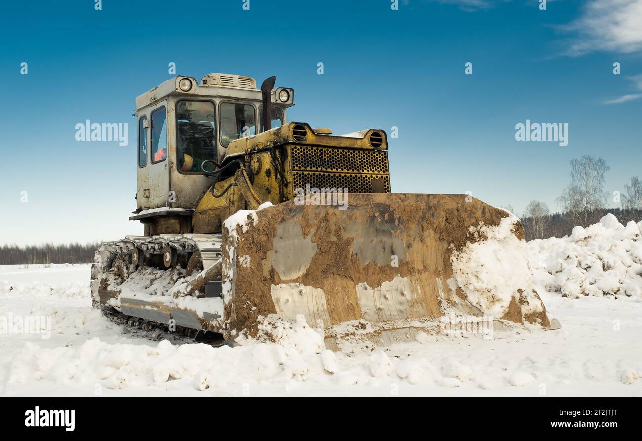 Yellow crawler tractor bulldozer with a bucket works in winter clearing ...