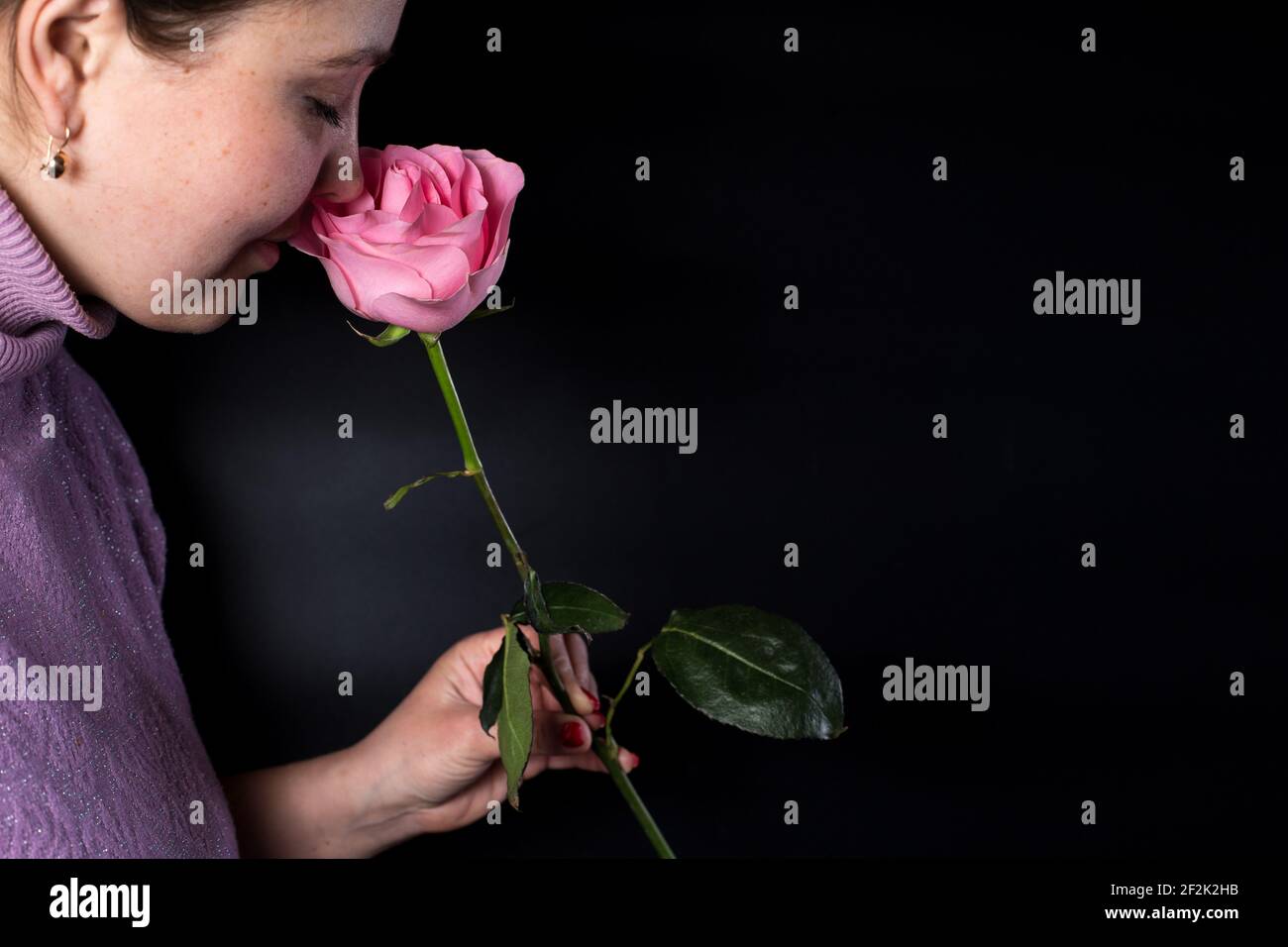 Fat young woman sniffing pink rose on black background with copy space ...