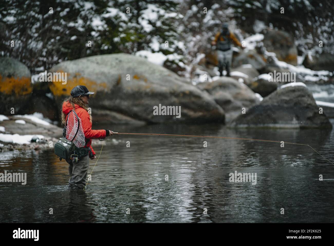 Side view of woman fly fishing while standing in river during winter ...