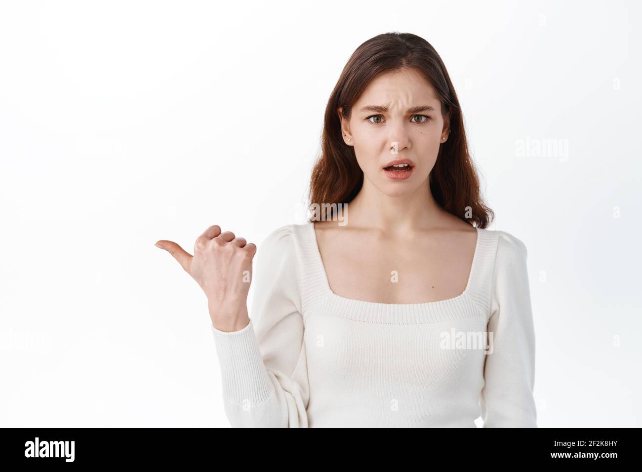 Confused young woman pointing aside at strange banner, stare at camera ...