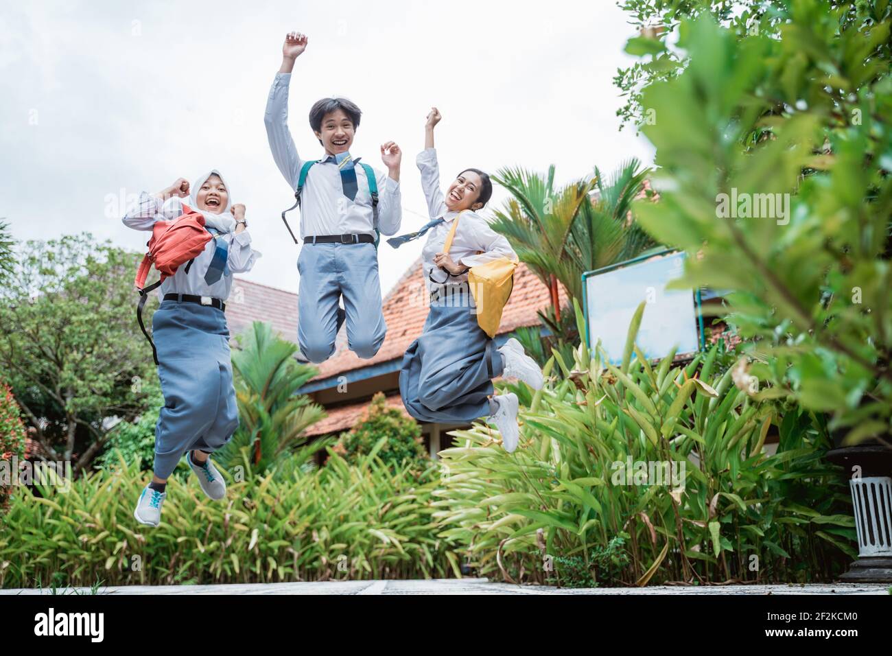 three high school students jumping high wearing school bags raising ...