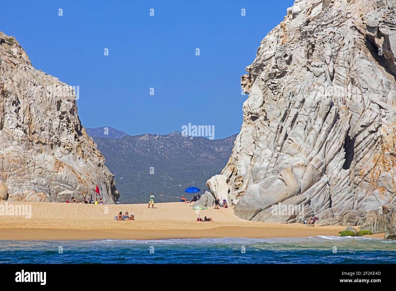 Limestone sea cliffs and tourists sunbathing on secluded beach near the ...