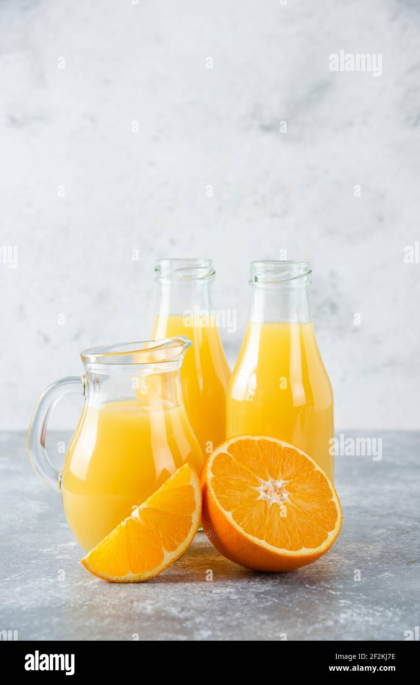 A glass pitcher of juice with fresh orange fruits on stone background ...