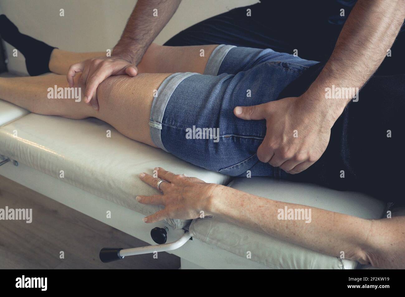 Hands of osteopath on hip and left knee of female patient lying on ...