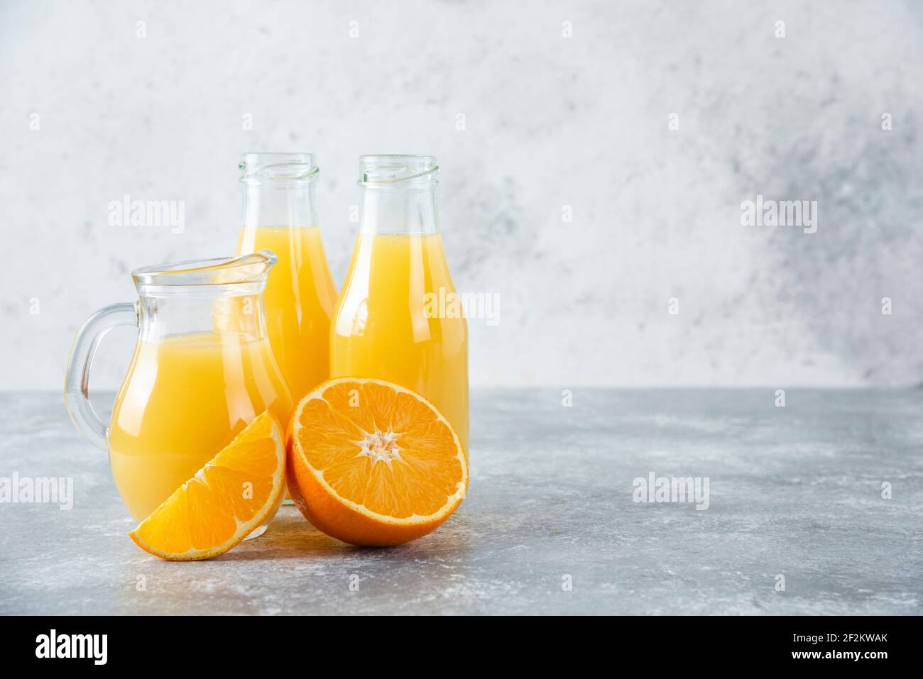 A glass pitcher of juice with fresh orange fruits on stone background ...