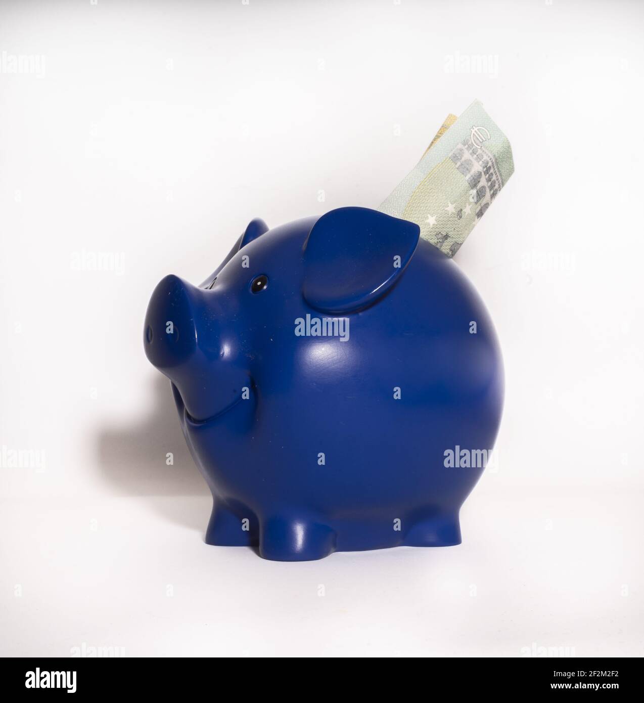 A closeup of cash money in a blue piggy bank isolated on a white ...