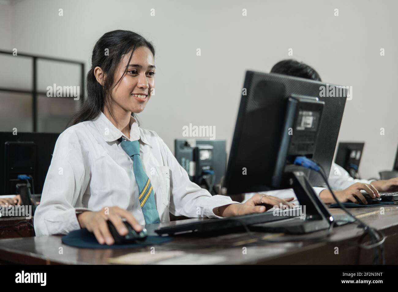 female high school students smile while using a computer pc with their ...