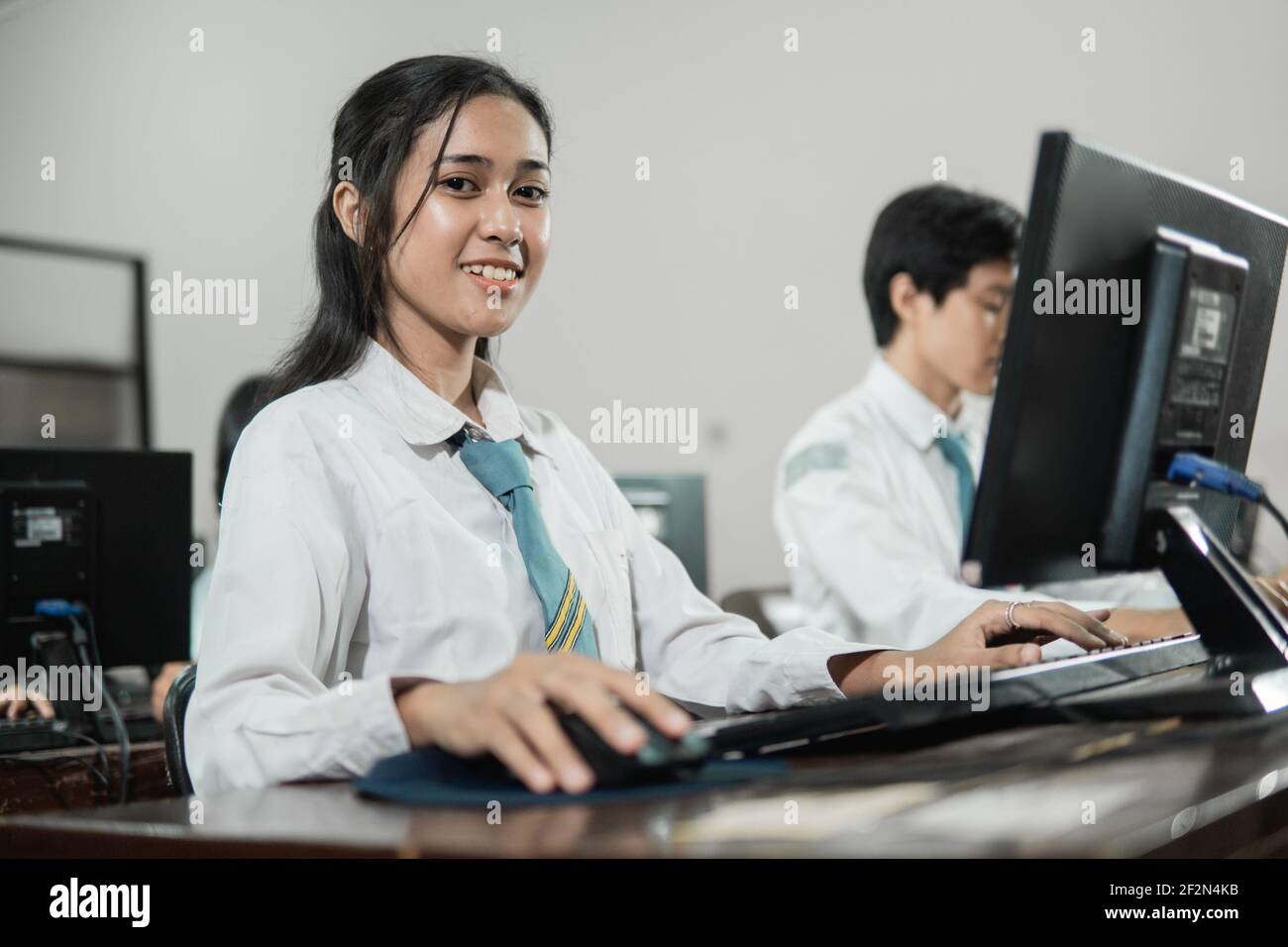 female high school students smile looking at the camera while using a ...