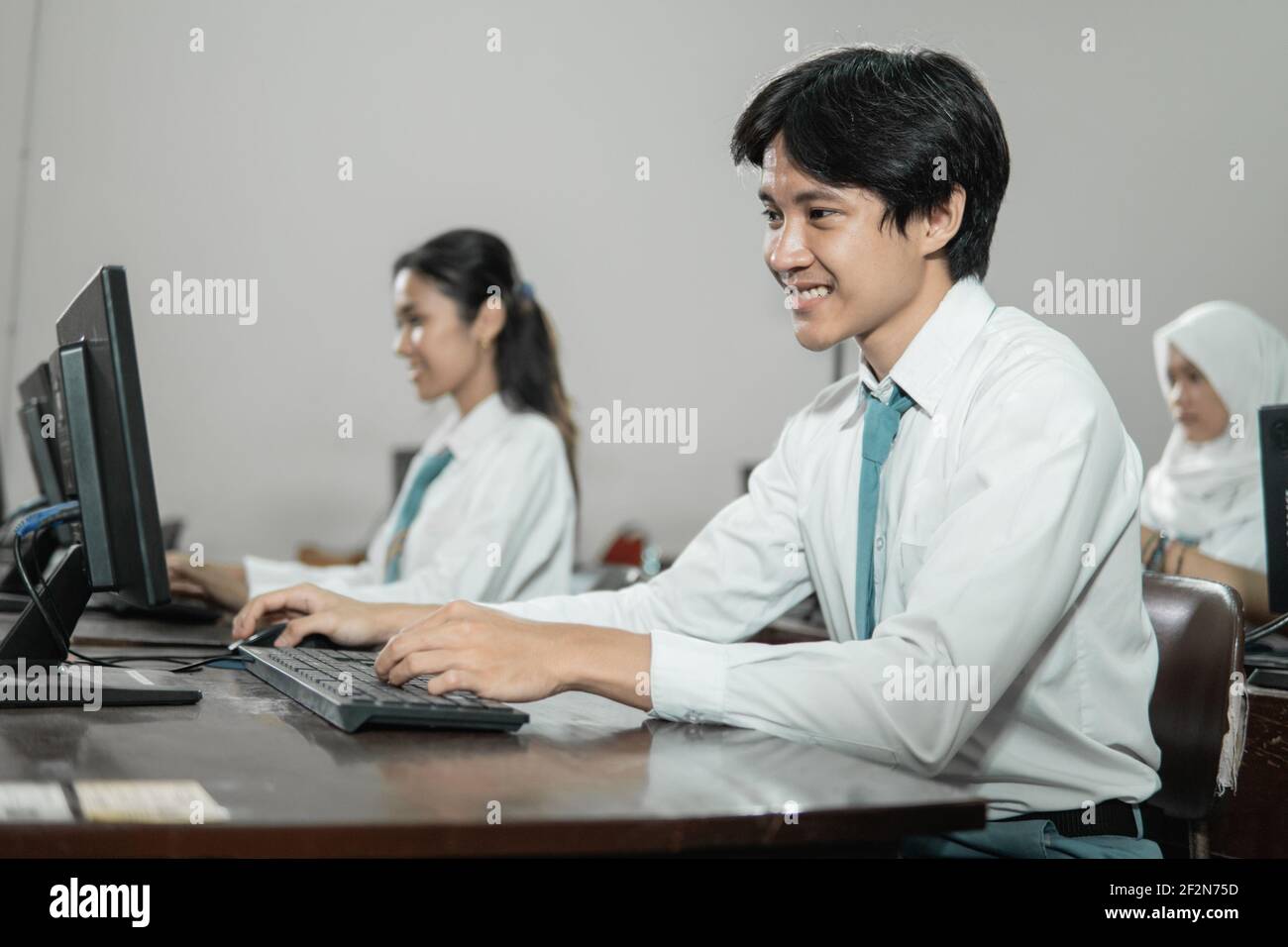 male high school students smile while using a computer pc with their ...