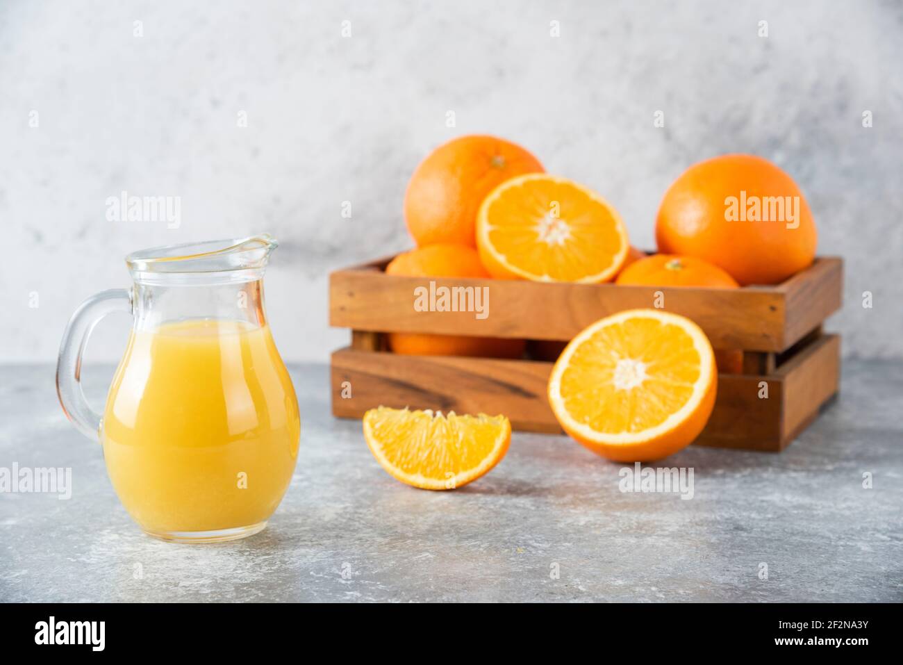 A glass pitcher of juice with fresh orange fruits on stone background ...