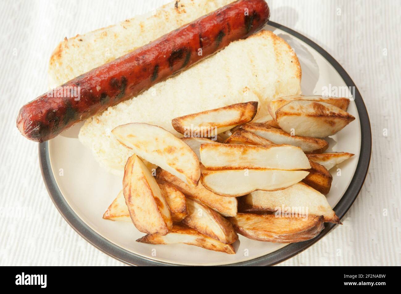 A tasty hotdog with baked potatoes on a plate Stock Photo - Alamy