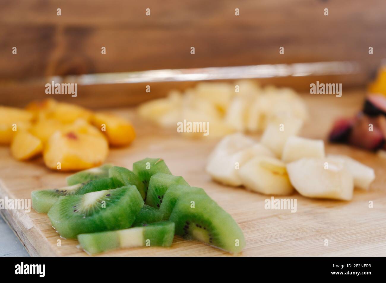 Chopped fruits arranged on cutting board on white wooden background ...