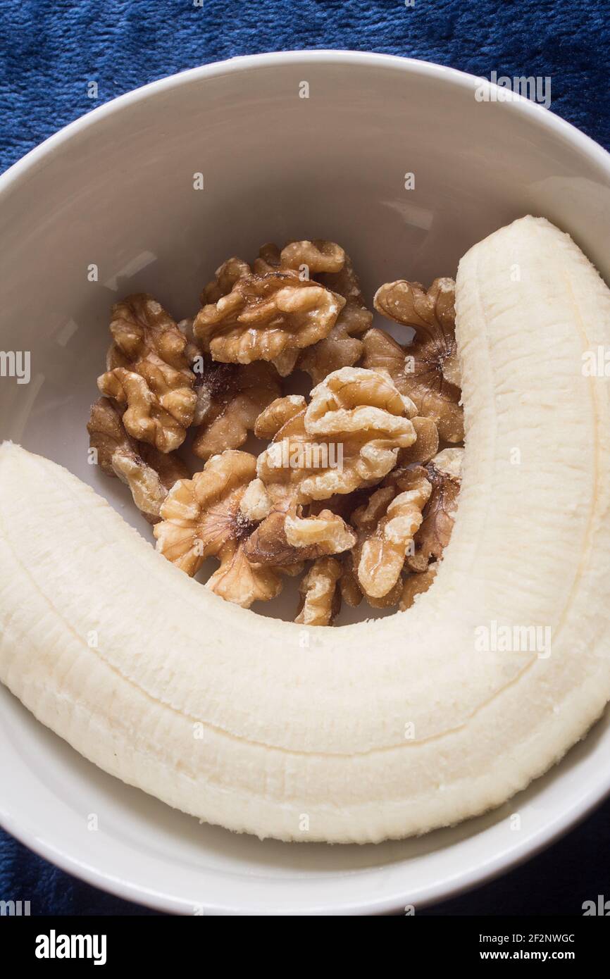 A white bowl with a handful of walnuts and a peeled banana next to it ...