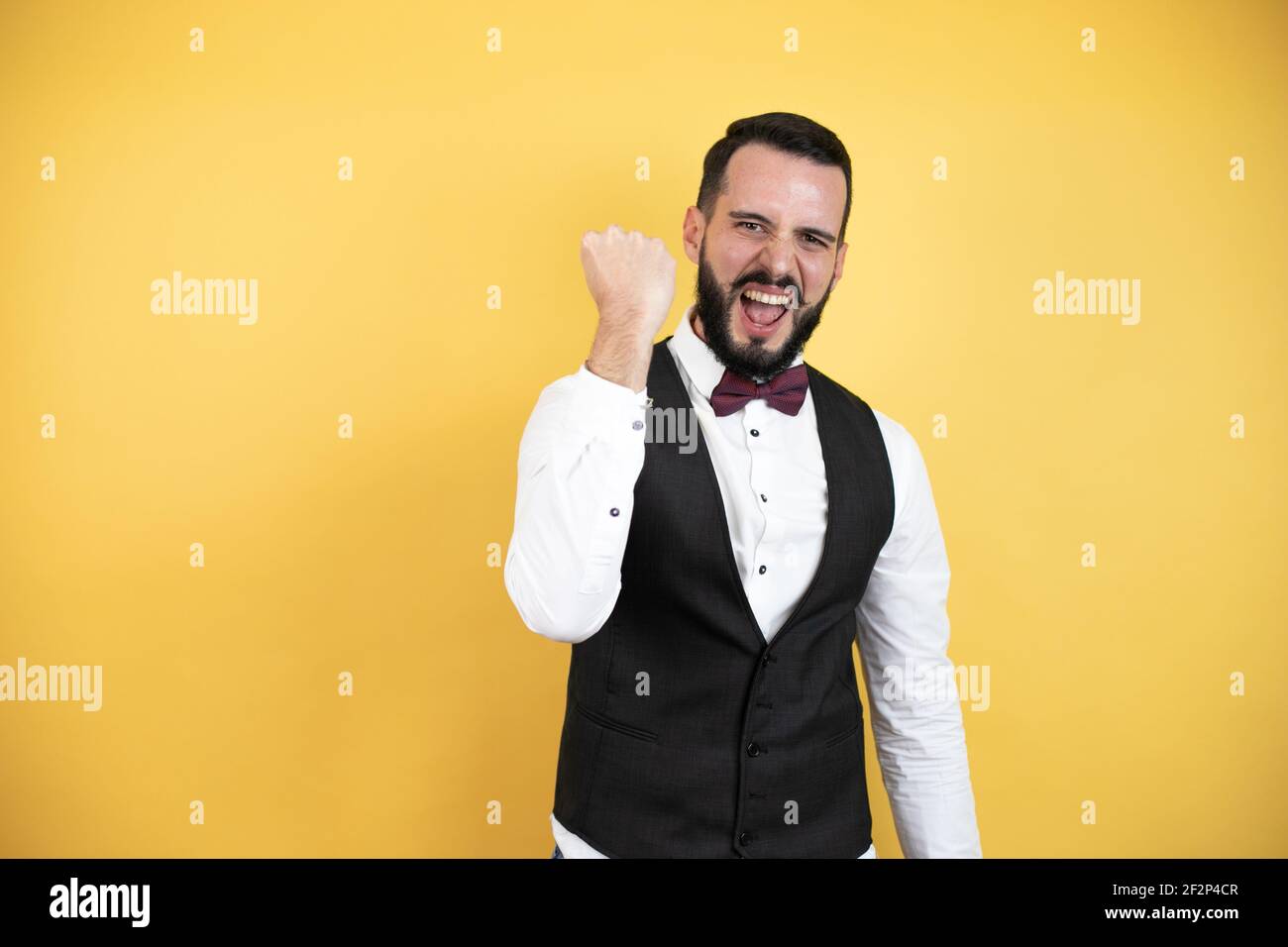 Young man with beard wearing bow tie and vest angry and mad raising ...