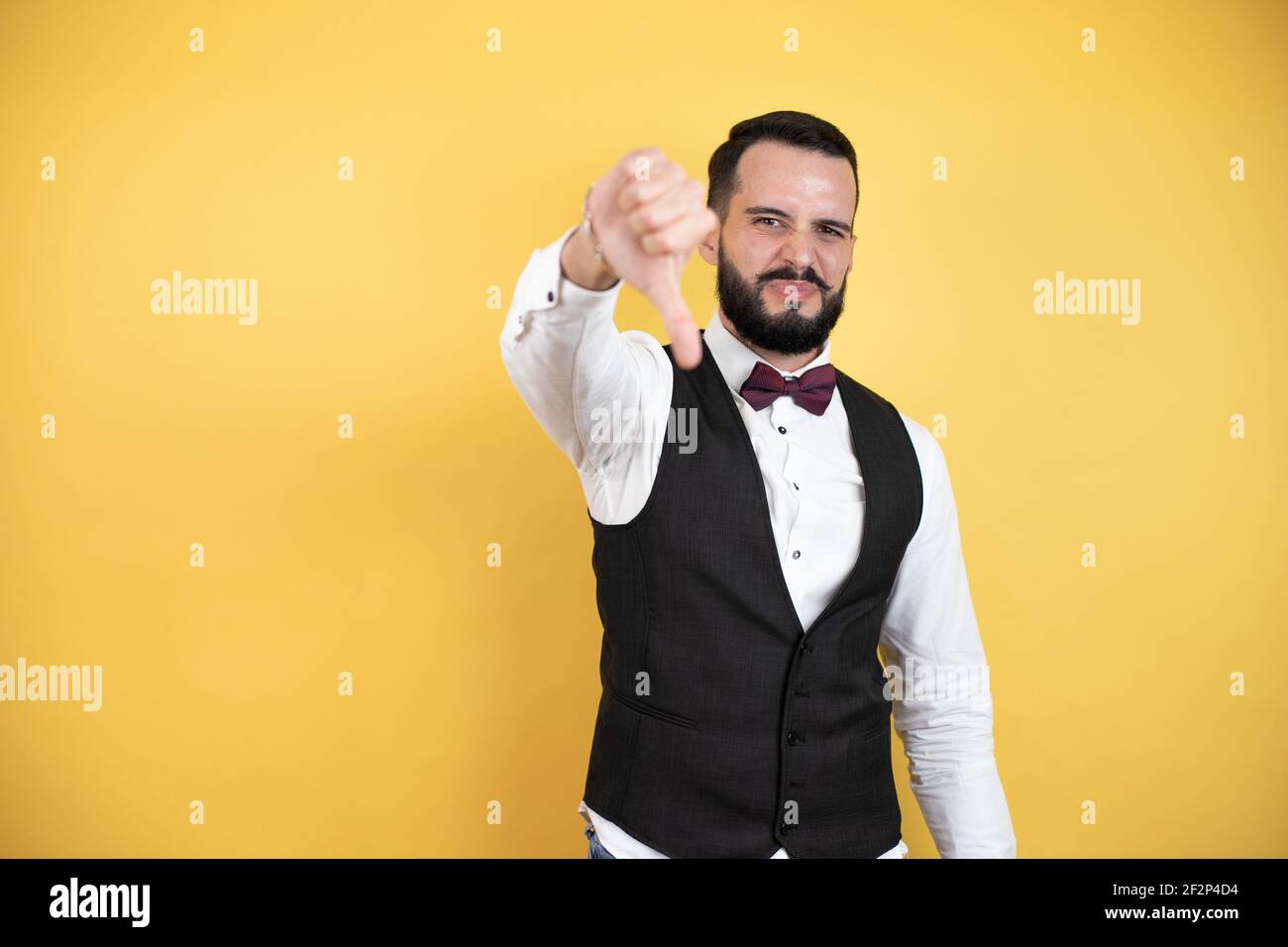 Young man with beard wearing bow tie and vest with angry face, negative ...