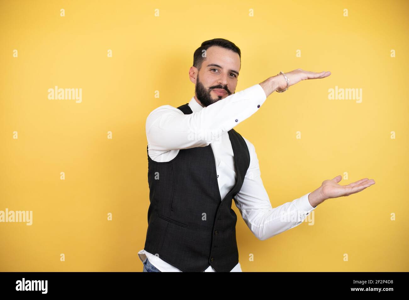 Young man with beard wearing bow tie and vest gesturing with hands ...