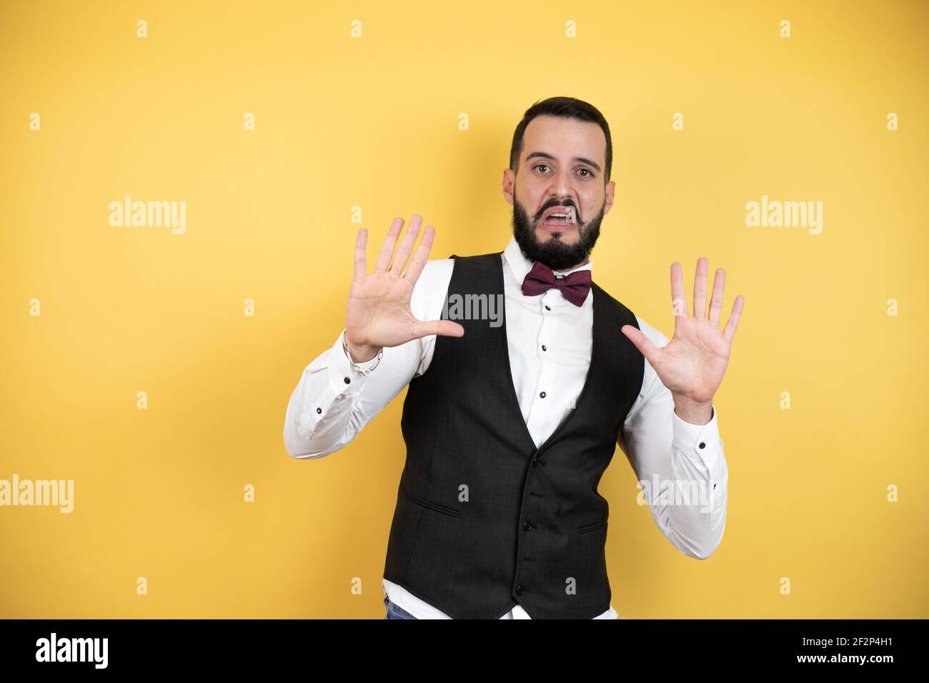 Young man with beard wearing bow tie and vest afraid and terrified with ...
